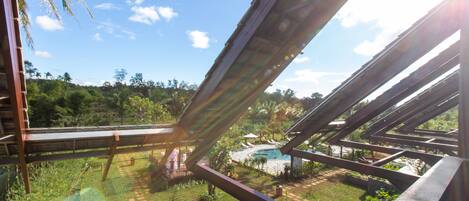 Vista de um ponto alto, com vista para área de piscina, céu limpo e vegetação exuberante.