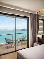 Quarto de hotel com varanda, cama, cadeira, mesa e vista para o mar.