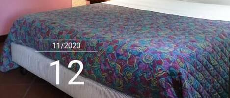 Quarto de hotel com uma cama, mesa de cabeceira, relógio de parede e uma pintura.