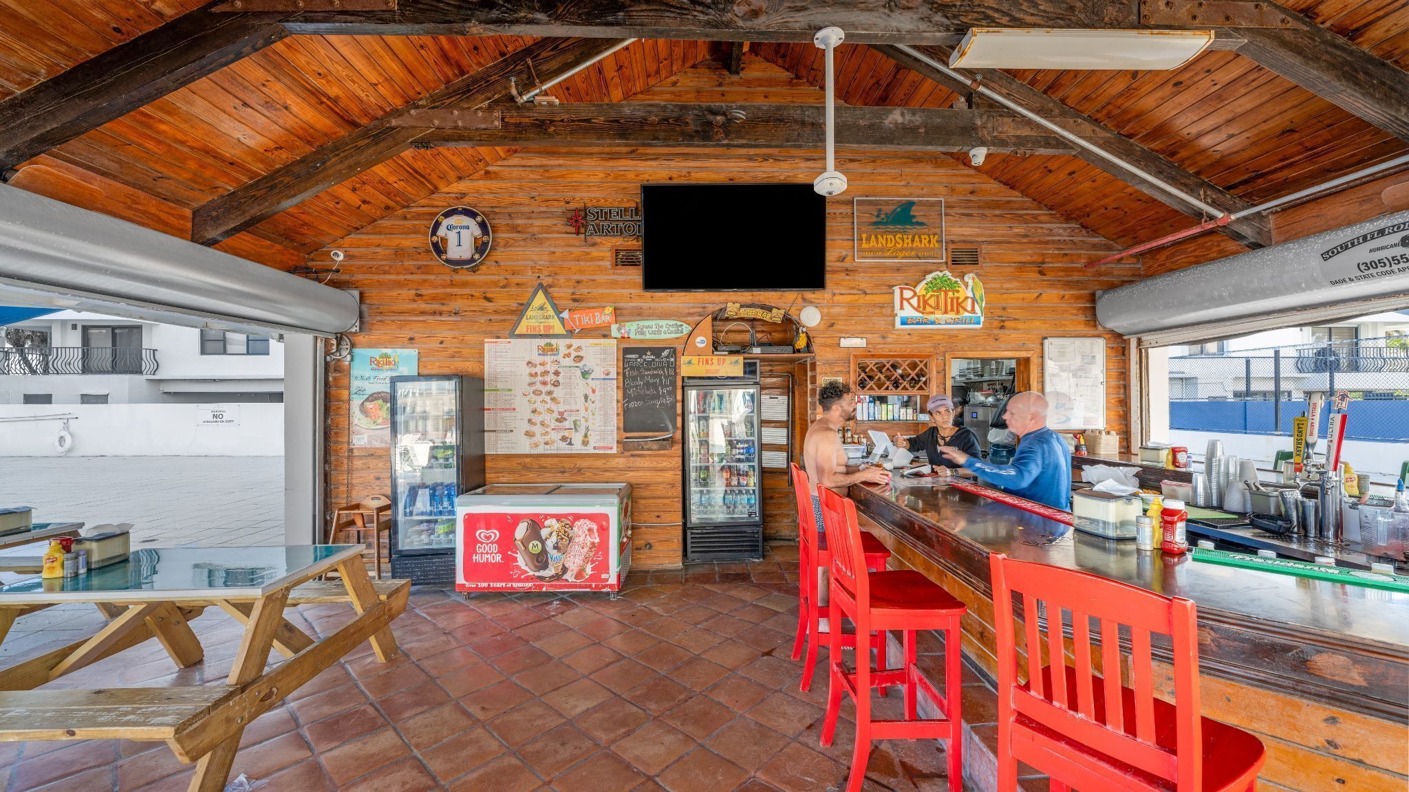 Restaurante com decoração em madeira, área de bar e um painel de cardápio.