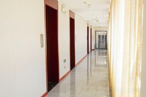 Corredor longo e estreito em hotel, com portas de um lado e uma parede lisa do outro.