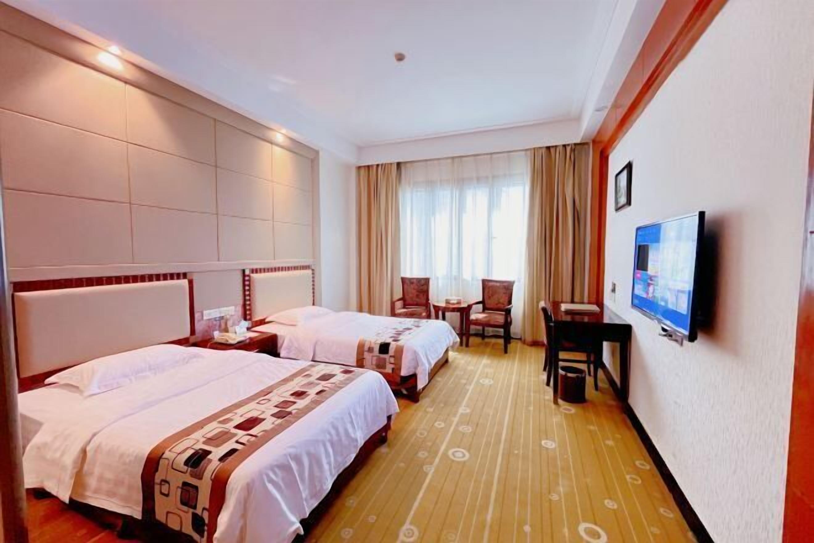 Quarto de hotel com duas camas, televisão, uma mesinha e uma cadeira.