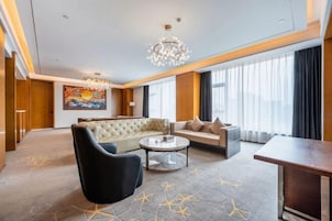 Um saguão de hotel moderno com um conjunto de sofás, uma mesa de centro redonda e um candelabro.