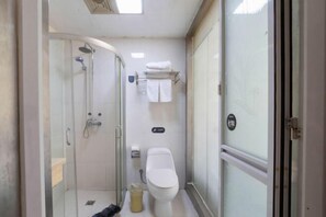 Casa de banho compacta com cabine de chuveiro em vidro, sanita e barra de toalhas.