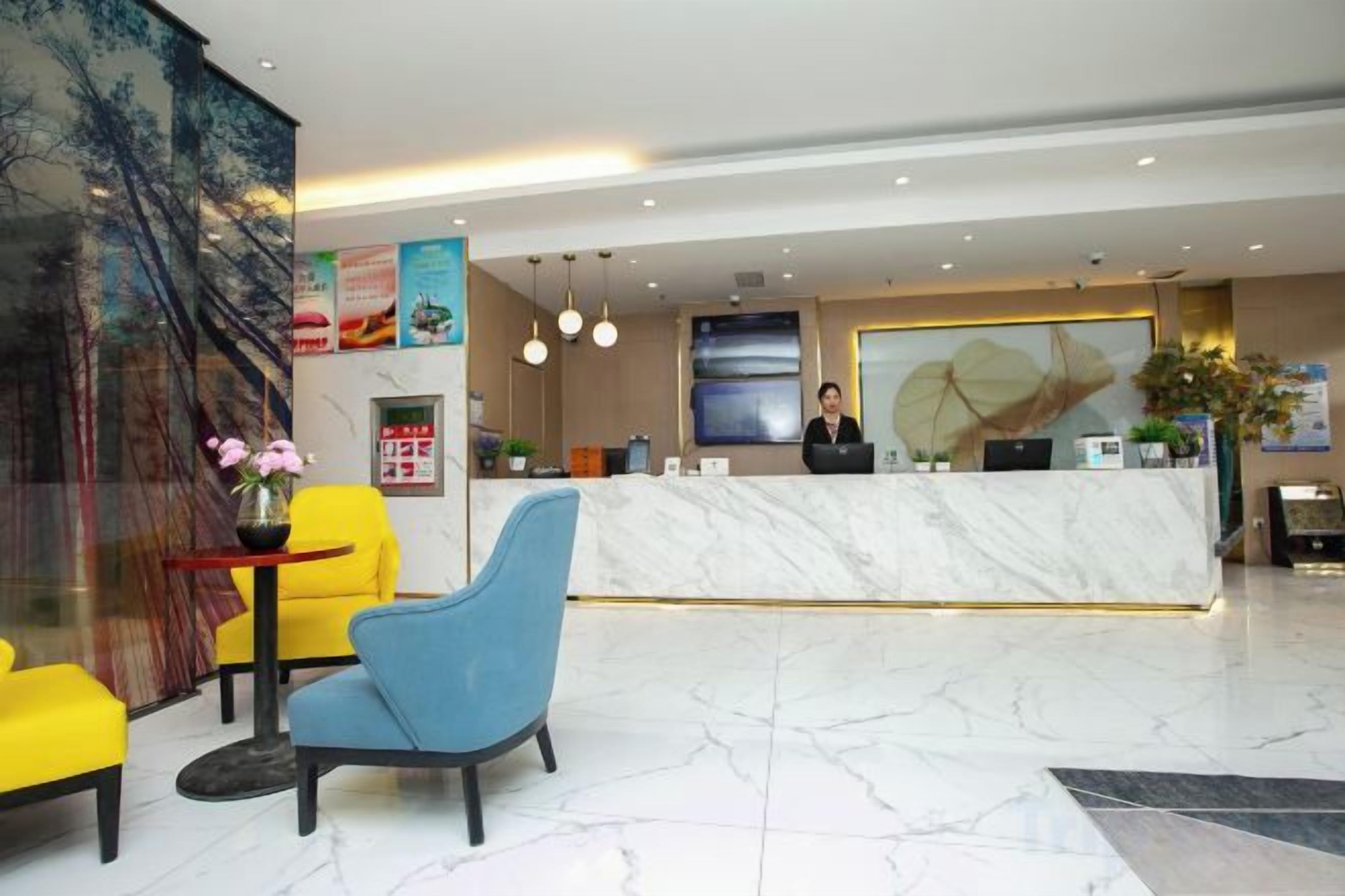 Recepção de hotel com balcão de mármore, recepcionista e área de estar.