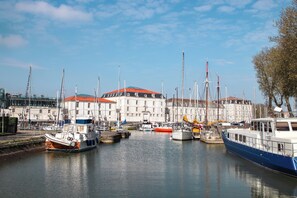 Uma marina com vários barcos atracados, um edifício grande com telhado vermelho e um céu limpo.