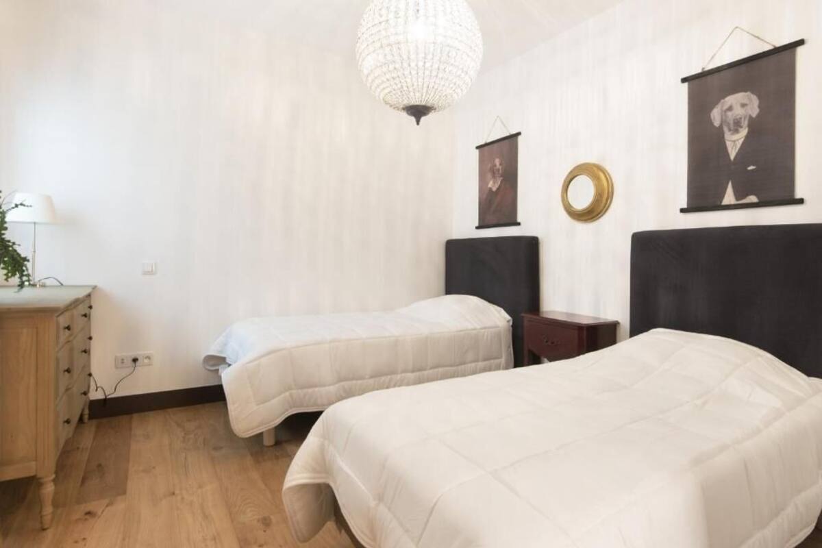 Quarto com duas camas, cômoda de madeira, candelabro e quadros nas paredes.