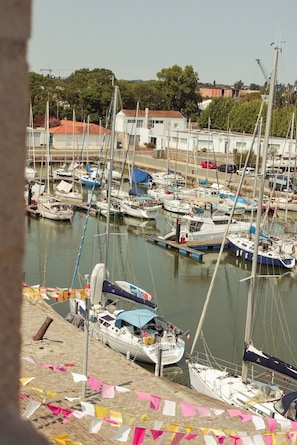 Uma marina com vários veleiros atracados, um calçadão pavimentado e edifícios ao fundo.
