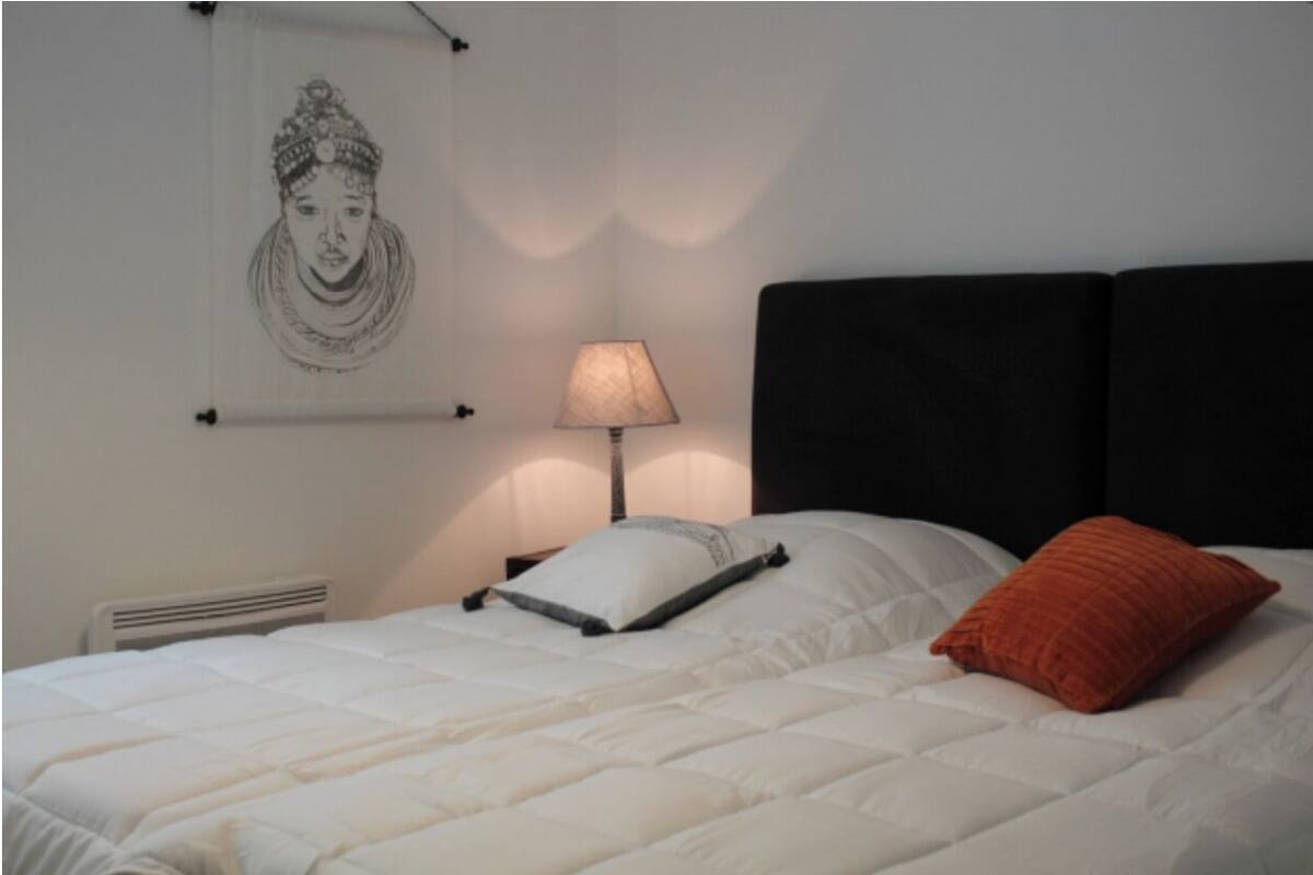 Um quarto com cama, mesa de cabeceira, luminária e um objeto pendurado na parede.