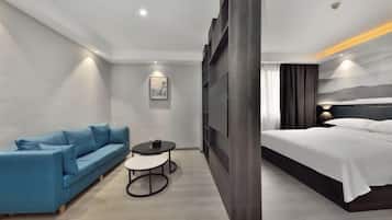 Quarto de hotel moderno com sofá, mesa redonda pequena, cama e televisão.