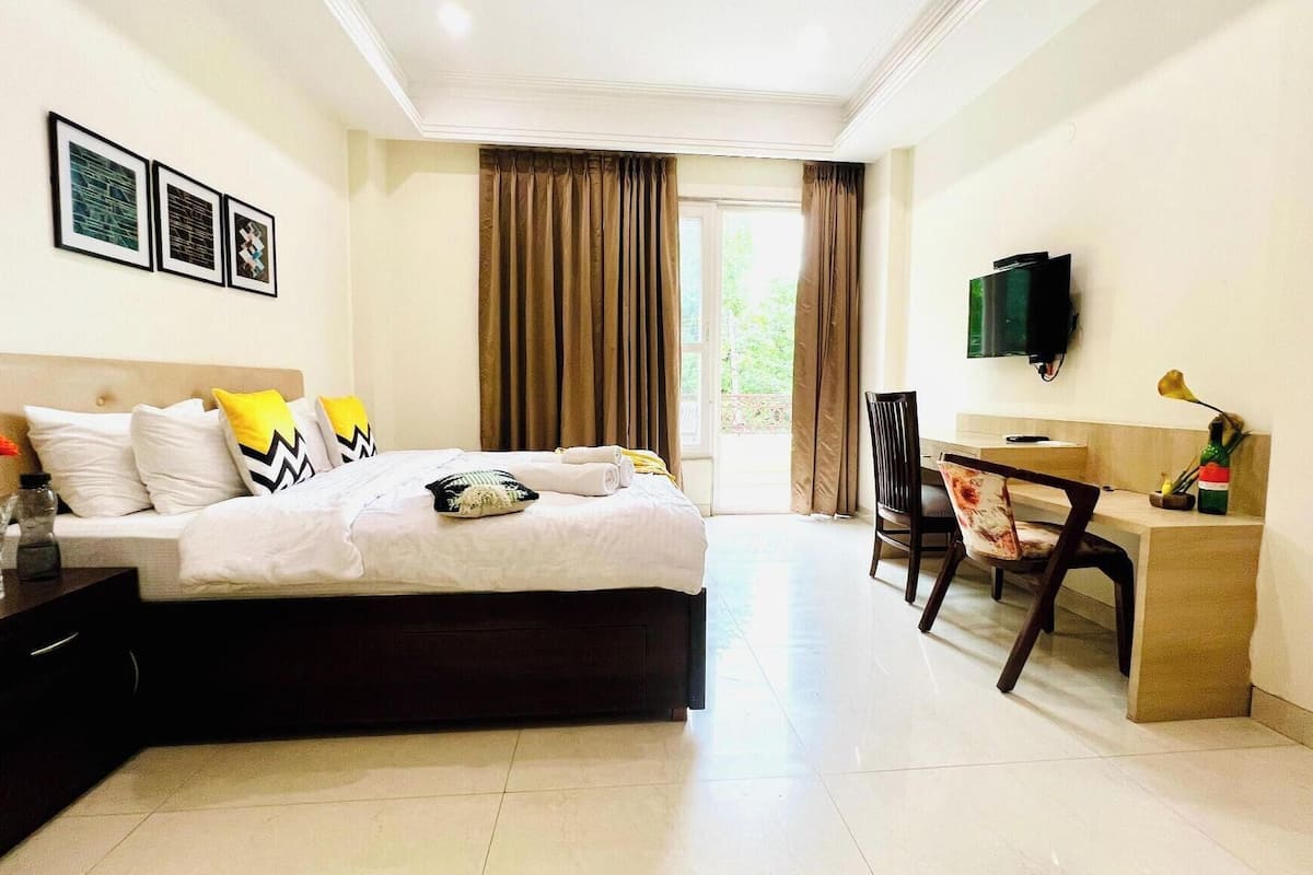 Quarto de hotel com cama, escrivaninha, cadeira, televisão e janela com cortinas.