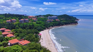 Um resort costeiro com vários edifícios, uma praia de areia e vista para o mar.