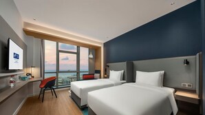 Quarto de hotel com duas camas, televisão, escrivaninha e uma cadeira, e vista para o mar.