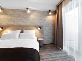 Quarto de hotel moderno com parede texturizada em tijolos, cabeceira de madeira e mesa de cabeceira redonda.
