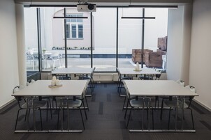 Sala de conferências com mesas, cadeiras, janelas amplas e um projetor.