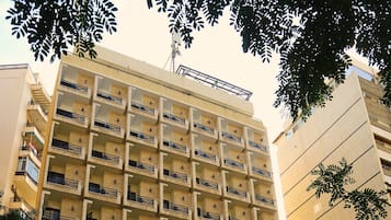 Um hotel com várias andares, varandas, uma bandeira e carros estacionados.