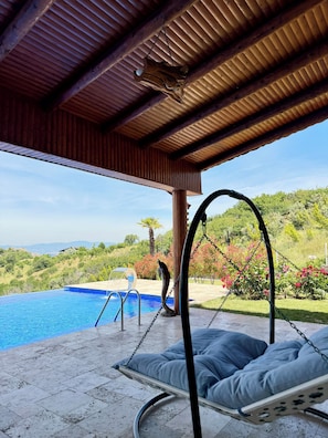 Área externa coberta com piscina, cadeira de balanço e vista para a paisagem.