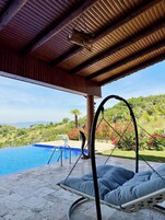 Área externa coberta com piscina, cadeira de balanço e vista para a paisagem.
