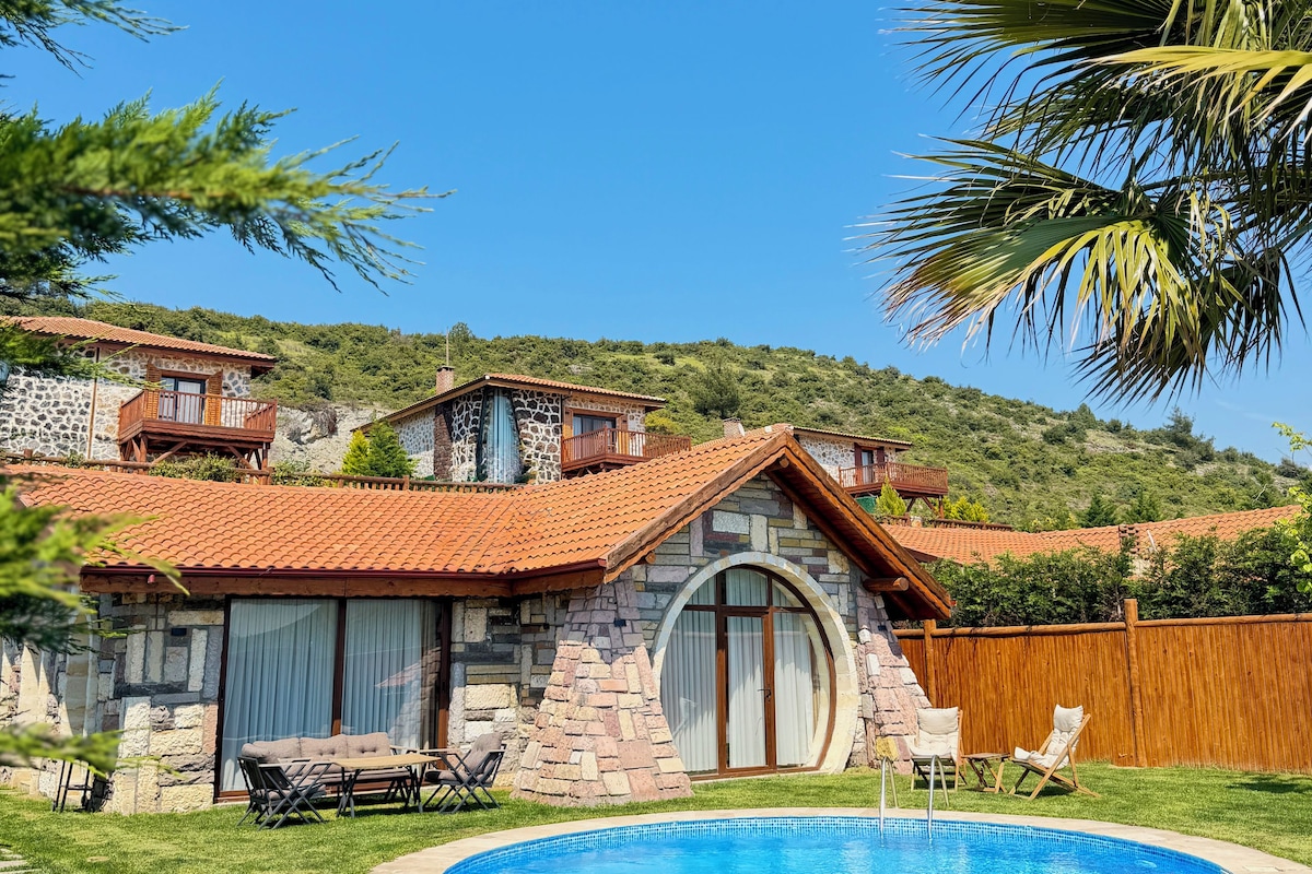 Uma casa de pedra com telhado de telhas, piscina e deck de madeira.