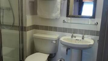 Casa de banho com cabine de duche em vidro, sanita, lavatório e um porta-toalhas com toalhas dobradas.