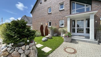 Uma casa moderna de dois andares com fachada de tijolos, varanda frontal e um jardim bem cuidado com pedras e plantas.