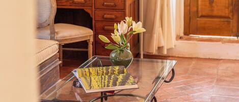 Quarto com escrivaninha de madeira, mesa de centro de vidro com um livro e flores, um mapa-múndi na parede e uma porta de madeira.