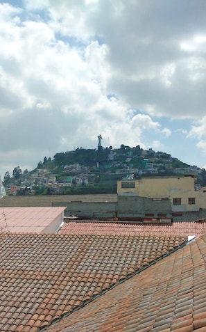 Vista de uma área montanhosa com uma estátua no topo, um edifício com telhado de cerâmica em primeiro plano e um céu nublado.