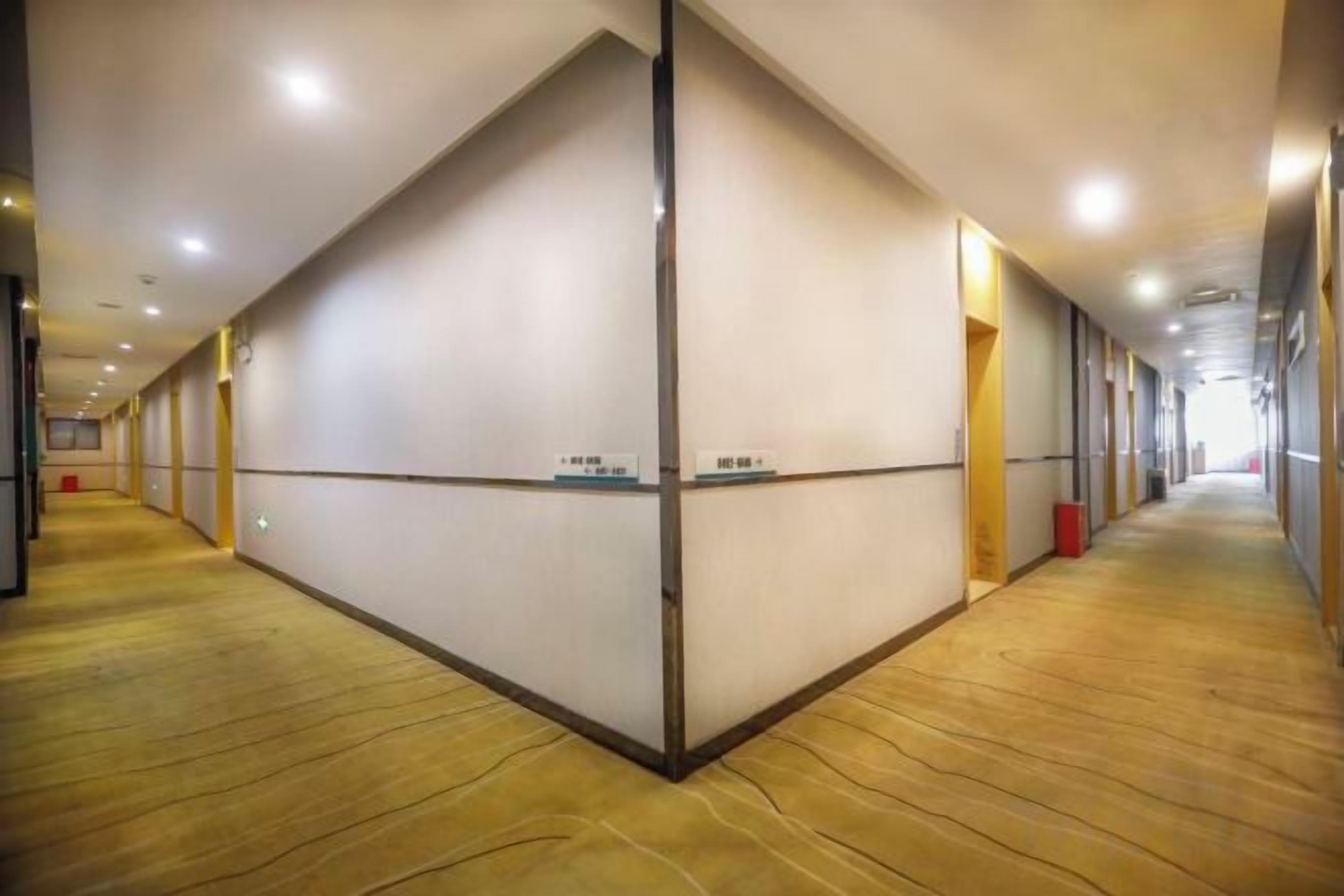 Um corredor com piso de madeira, uma parede divisória e uma porta à direita.