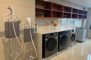 Área de lavanderia com máquina de lavar, secadora e secador de cabelo.