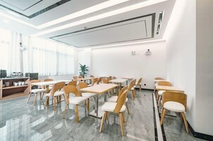 Uma sala de conferências moderna, com mesas, cadeiras, um quadro branco e uma planta.