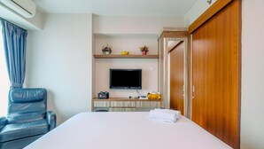 Quarto de hotel com cama, televisão, secretária com computador, cadeira e guarda-roupa.