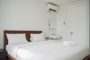 Cama bem arrumada com lençóis brancos, cabeceira de madeira, mesa de cabeceira, ar condicionado branco fixado na parede, espelho pequeno ao lado da cama e uma toalha sobre a cama.