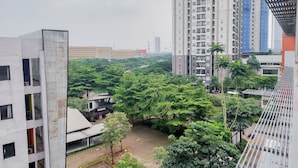 Um edifício alto com vários andares, um pátio com árvores e vista para outros edifícios ao fundo.