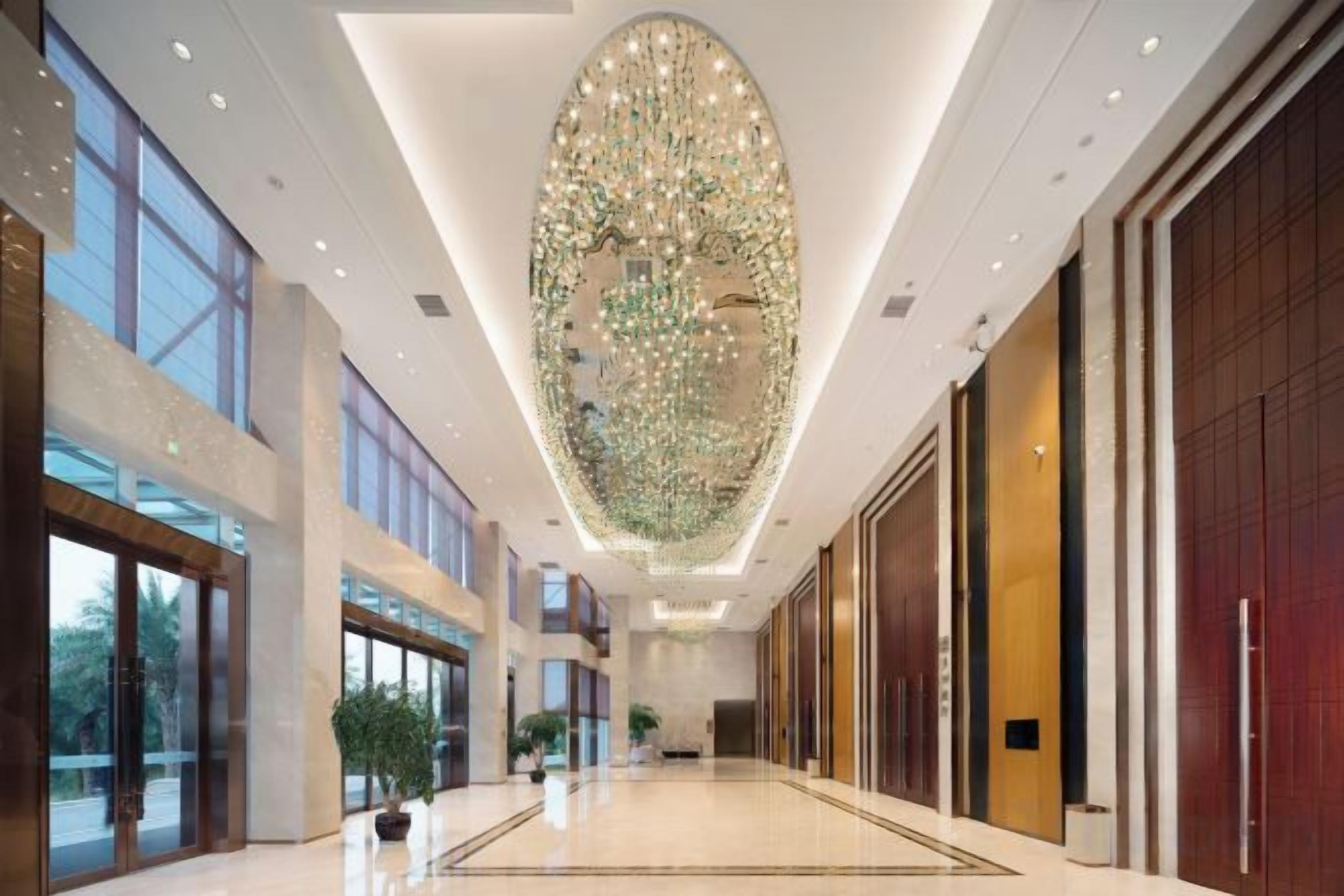 Um amplo hall de hotel com um lustre grande, várias portas e plantas em vasos.