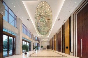 Um amplo hall de hotel com um lustre grande, várias portas e plantas em vasos.