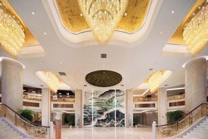 Um hall espaçoso com um lustre imponente, uma escadaria central e um grande mural.