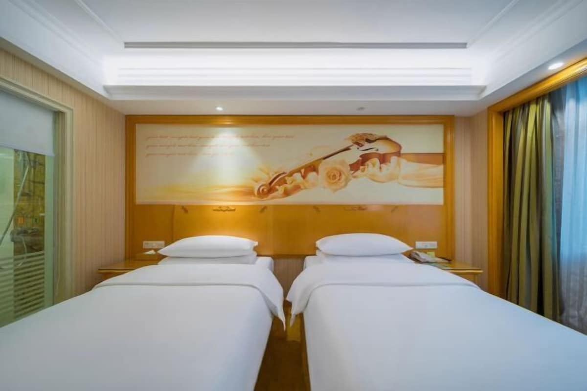 Quarto de hotel com duas camas, um grande mural na parede e uma cabeceira de madeira.