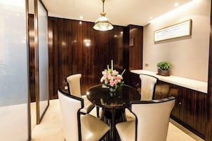Uma sala de conferências com uma mesa redonda, quatro cadeiras, um vaso de flores, um candelabro e um certificado emoldurado na parede.