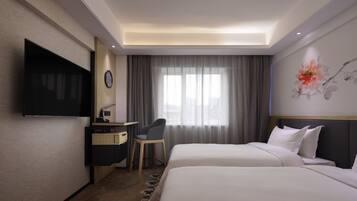 Quarto de hotel com televisão de tela plana, escrivaninha com cadeira, cama com roupa de cama branca, janela grande com cortinas e relógio fixado na parede.