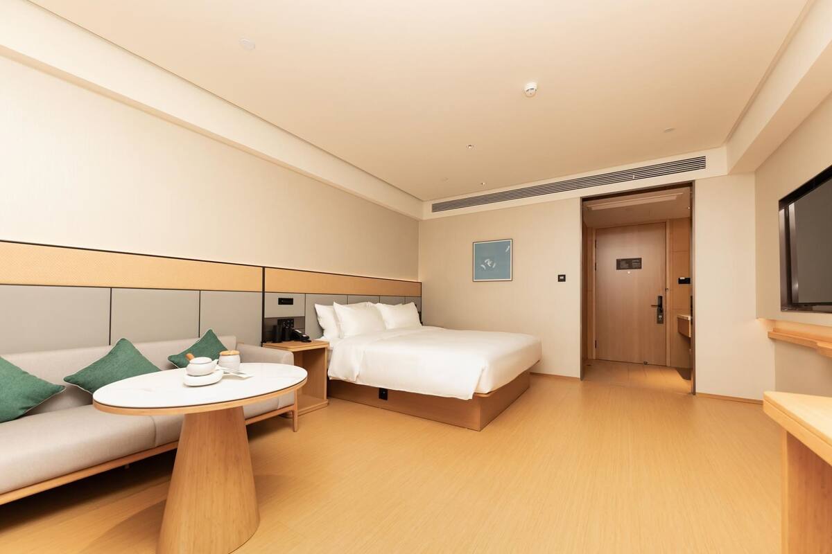 Quarto de hotel com cama, sofá, mesa redonda e televisão.
