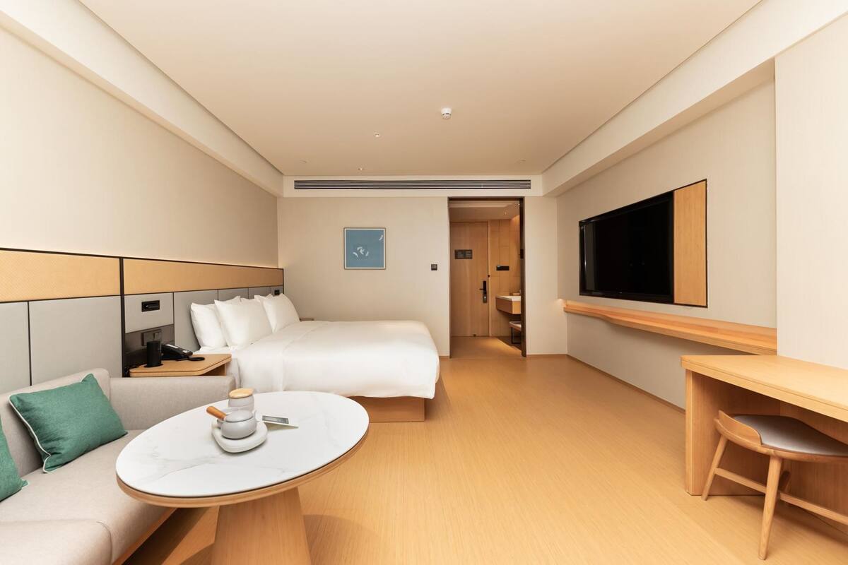 Quarto de hotel com cama, escrivaninha, televisão, mesa de centro e sofá.