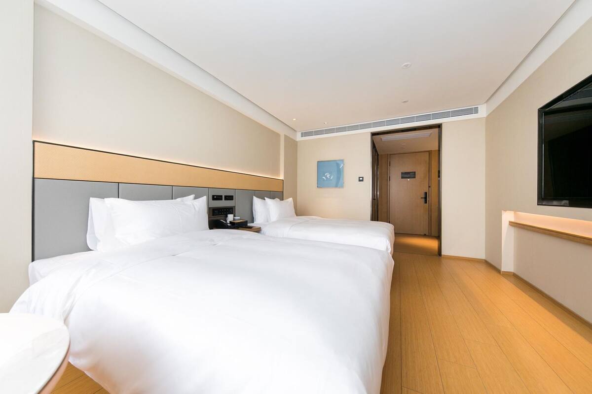 Quarto de hotel com duas camas, uma mesa de cabeceira, uma televisão e uma porta que dá para outro espaço.