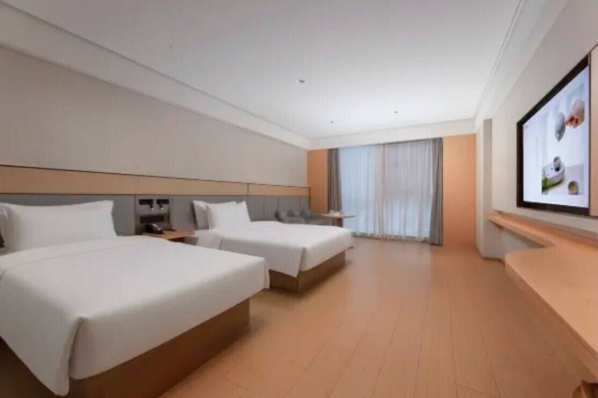 Quarto de hotel com duas camas, televisão, secretária e uma janela grande com cortinas.