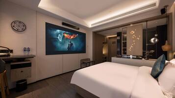 Quarto de hotel moderno com uma cama grande, uma TV de tela plana na parede, uma escrivaninha com cadeira e uma mesinha.
