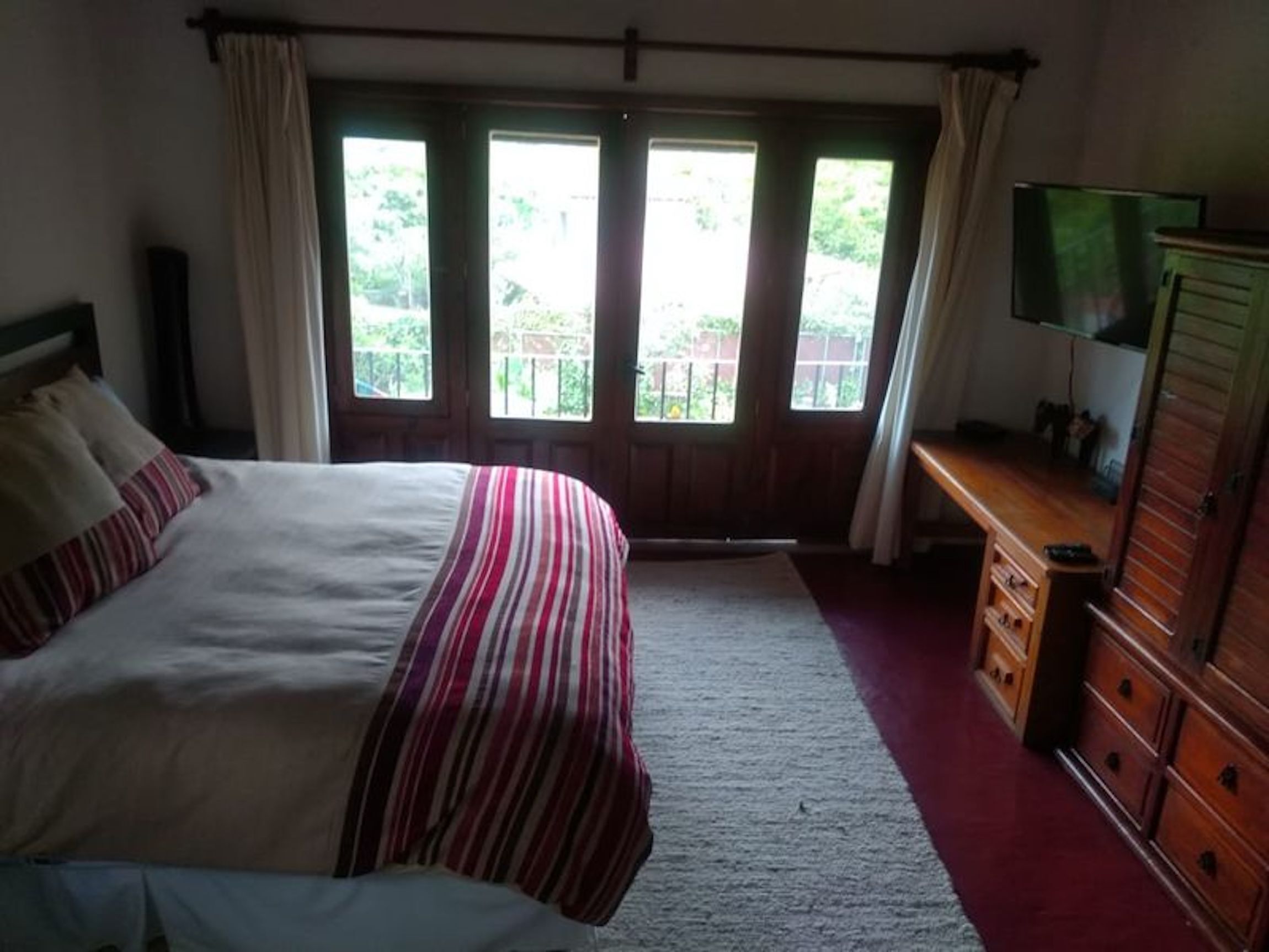 Quarto com cama, penteadeira, televisão e varanda com cortinas.