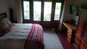Quarto com cama, penteadeira, televisão e varanda com cortinas.