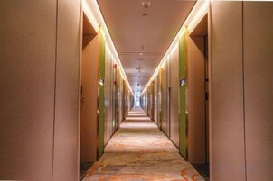 Corredor de hotel com portas em ambos os lados, carpete estampado e iluminação no teto.