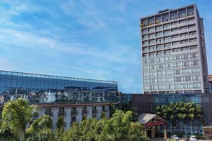 Um hotel moderno com fachada de vidro, um edifício tradicional com placa vermelha e um arranha-céu com muitas janelas.