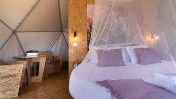 Um quarto em estilo de tenda aconchegante, com cama, uma mesinha e um espaço para sentar.