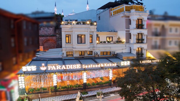 Um edifício de vários andares com um restaurante chamado "Paradise Seafood & Kebap" no andar térreo.